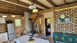 Interior em madeira com mesa de jantar, cadeiras, área de cozinha e parede de tijolos com um relógio.