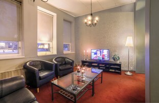 Uma sala de estar com mesa de centro de vidro, duas poltronas de couro, televisão e abajur.
