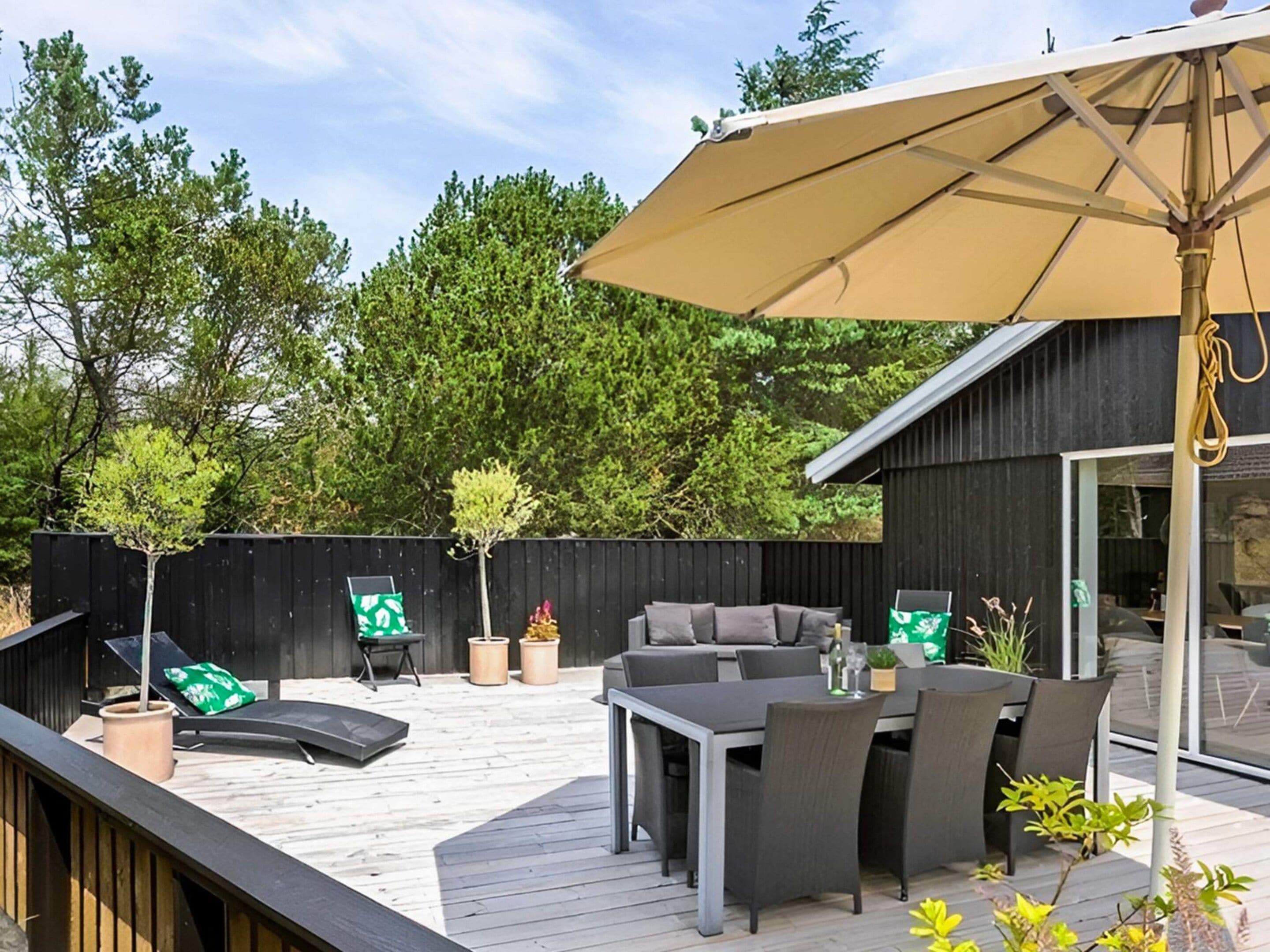 Um deck com móveis de exterior, churrasqueira e pergolado com guarda-sol.