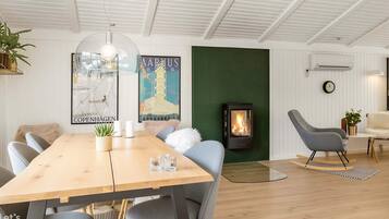 Uma sala de estar moderna com uma mesa de jantar de madeira, cadeiras cinzas, uma parede verde como destaque, uma lareira e um relógio fixado na parede.