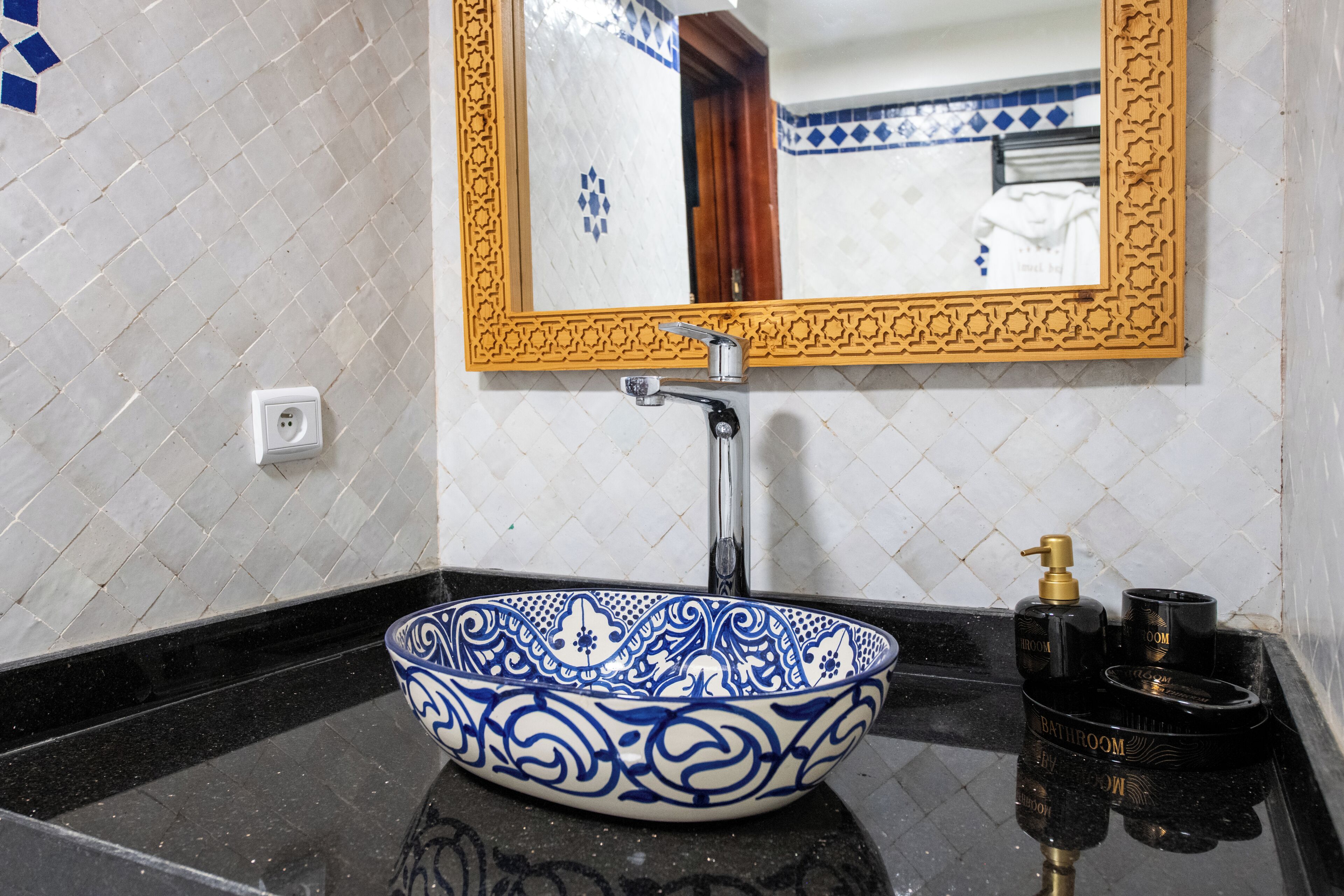 Um banheiro com uma pia preta, um espelho com moldura decorativa e uma tigela estampada em azul e branco.