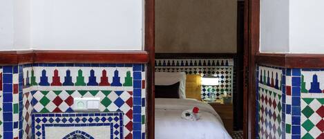 Quarto com uma cama, pia pequena e parede revestida por azulejos com padrão geométrico.