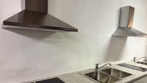 Cozinha moderna com pia de aço inoxidável, duas placas de indução e um exaustor.