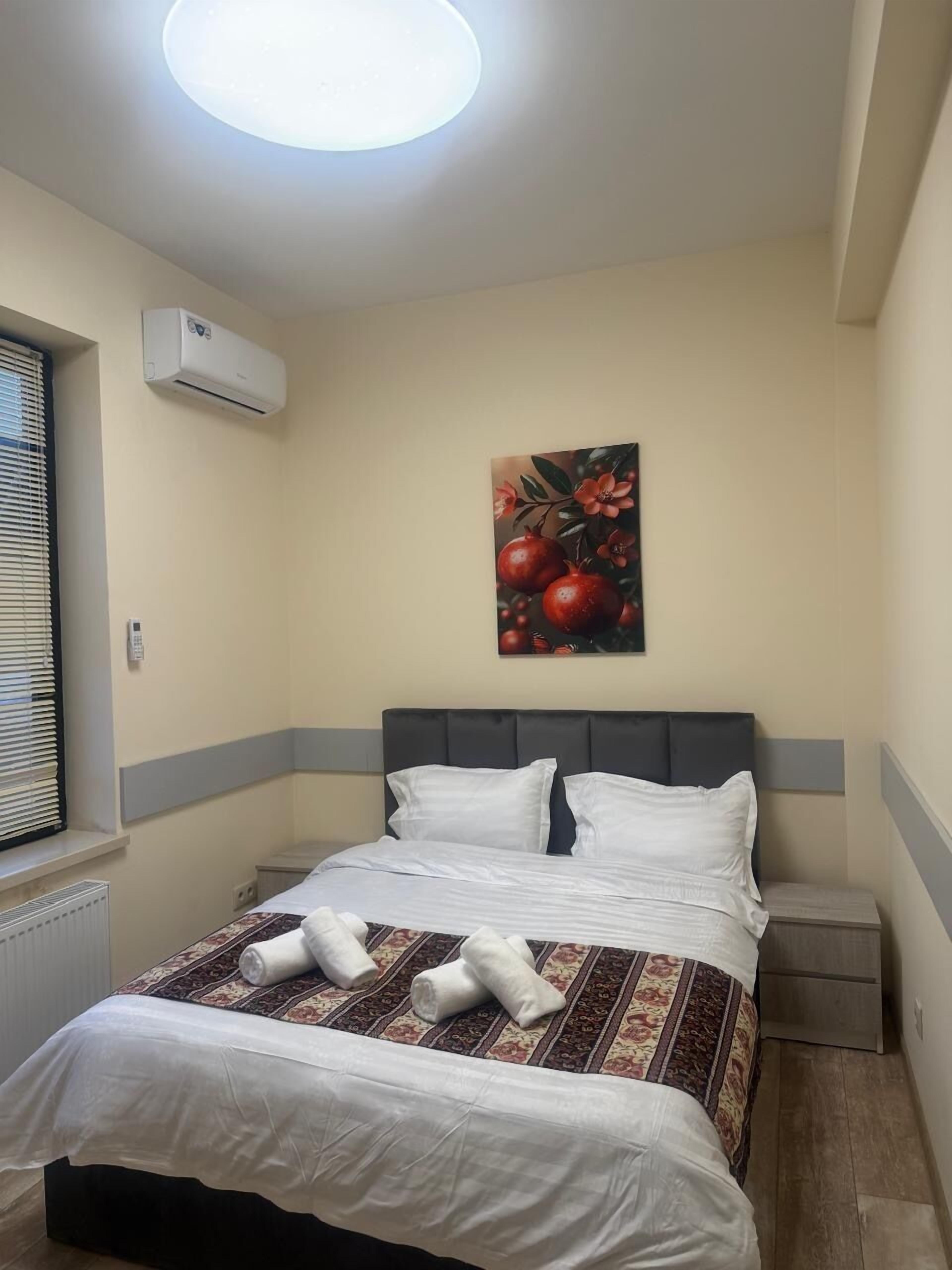 Quarto com cama, ar condicionado fixado na parede, janela com persianas e um quadro de romãs.
