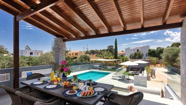 Uma área de refeições ao ar livre com vista para a piscina, móveis de vime e céu limpo.