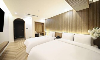 Quarto de hotel com duas camas, parede de painéis de madeira, televisão e corredor que dá para um armário.