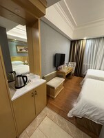 Quarto de hotel com cama, mesa de escritório com cadeira, televisão, chaleira e pequena mesa com controle remoto.