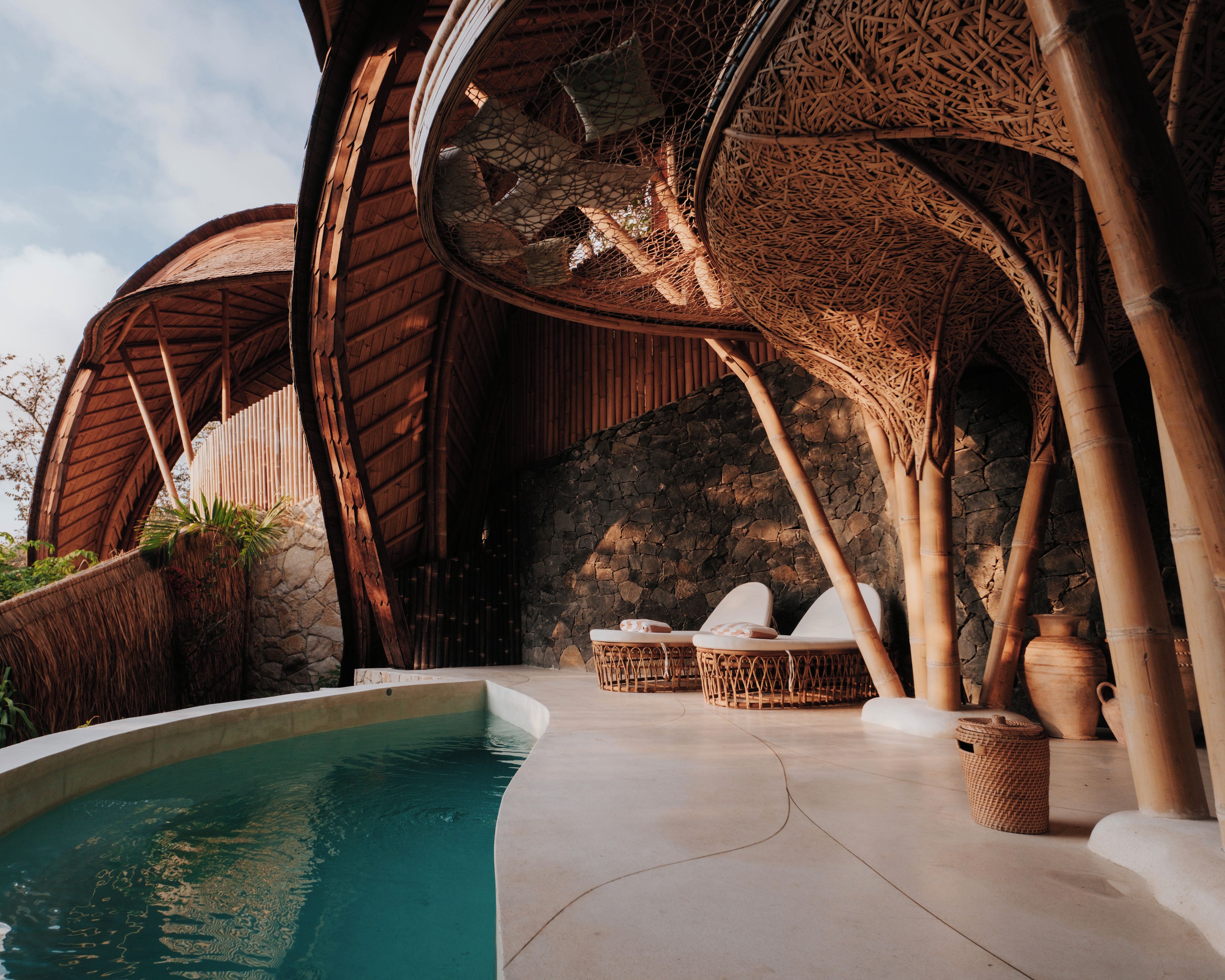 Área de piscina com muro de pedra e estruturas de bambu.