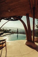 Área da piscina com vista para montanhas, uma pessoa perto da piscina e um espaço de estar coberto.