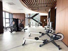 Uma academia moderna com diversos equipamentos de exercício, amplas janelas e teto de madeira.