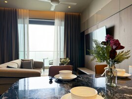 Quarto de hotel moderno com área de refeições, sofá, TV e vista para a cidade.
