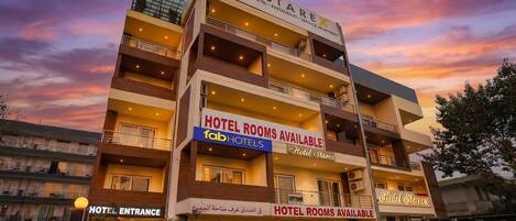 Um hotel com vários andares, varandas, uma placa indicando quartos disponíveis e uma entrada visível.