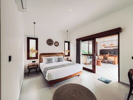 Quarto moderno com uma cama grande, uma mesa de cabeceira e vista para a cozinha por uma porta aberta.