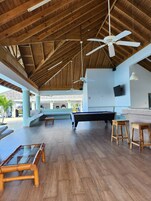 Um espaço amplo e coberto com mesa de bilhar, assentos e ventiladores de teto.
