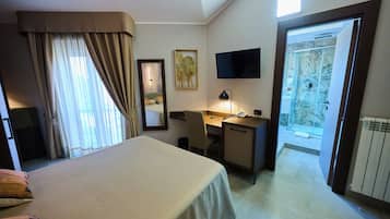 Quarto de hotel com cama, escrivaninha, cadeira, televisão e vista para uma varanda.