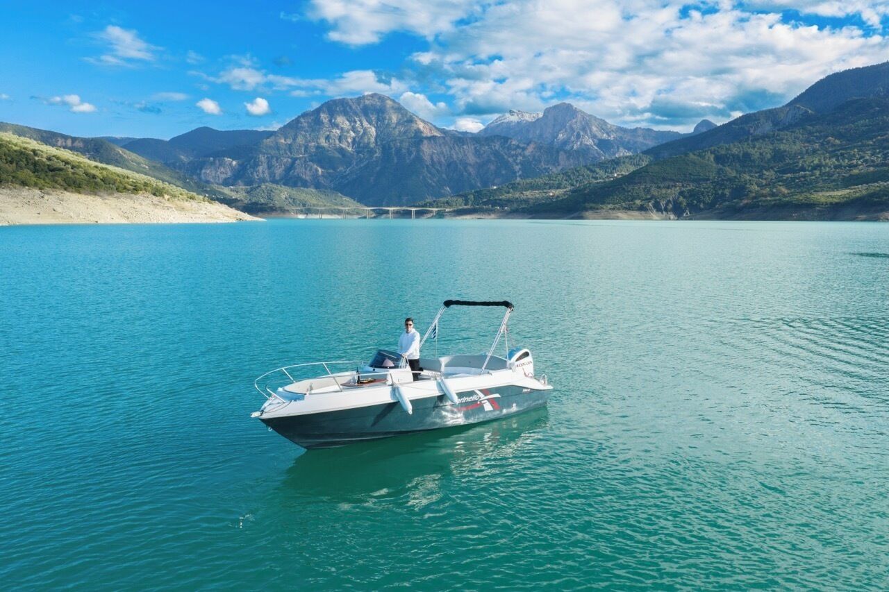 Um pequeno barco a motor num lago calmo, com montanhas ao fundo.