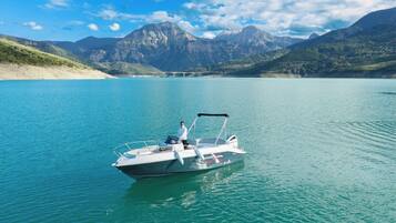 Um pequeno barco a motor num lago calmo, com montanhas ao fundo.
