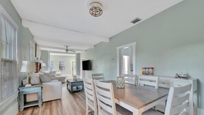 Uma sala de estar ampla com área de jantar, televisão na parede e um candelabro.