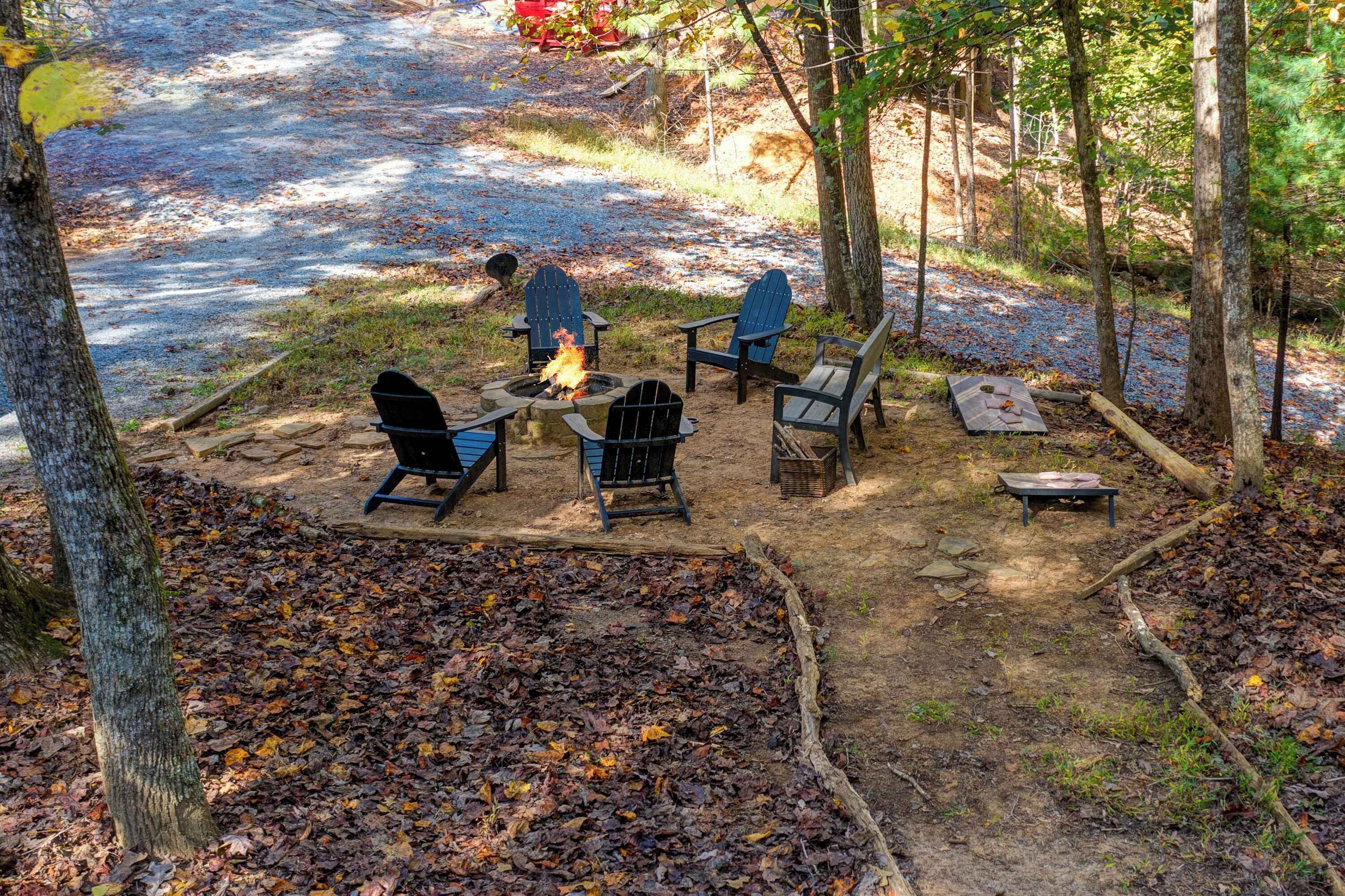 Um camping com lareira, quatro cadeiras Adirondack e uma mesa de piquenique.