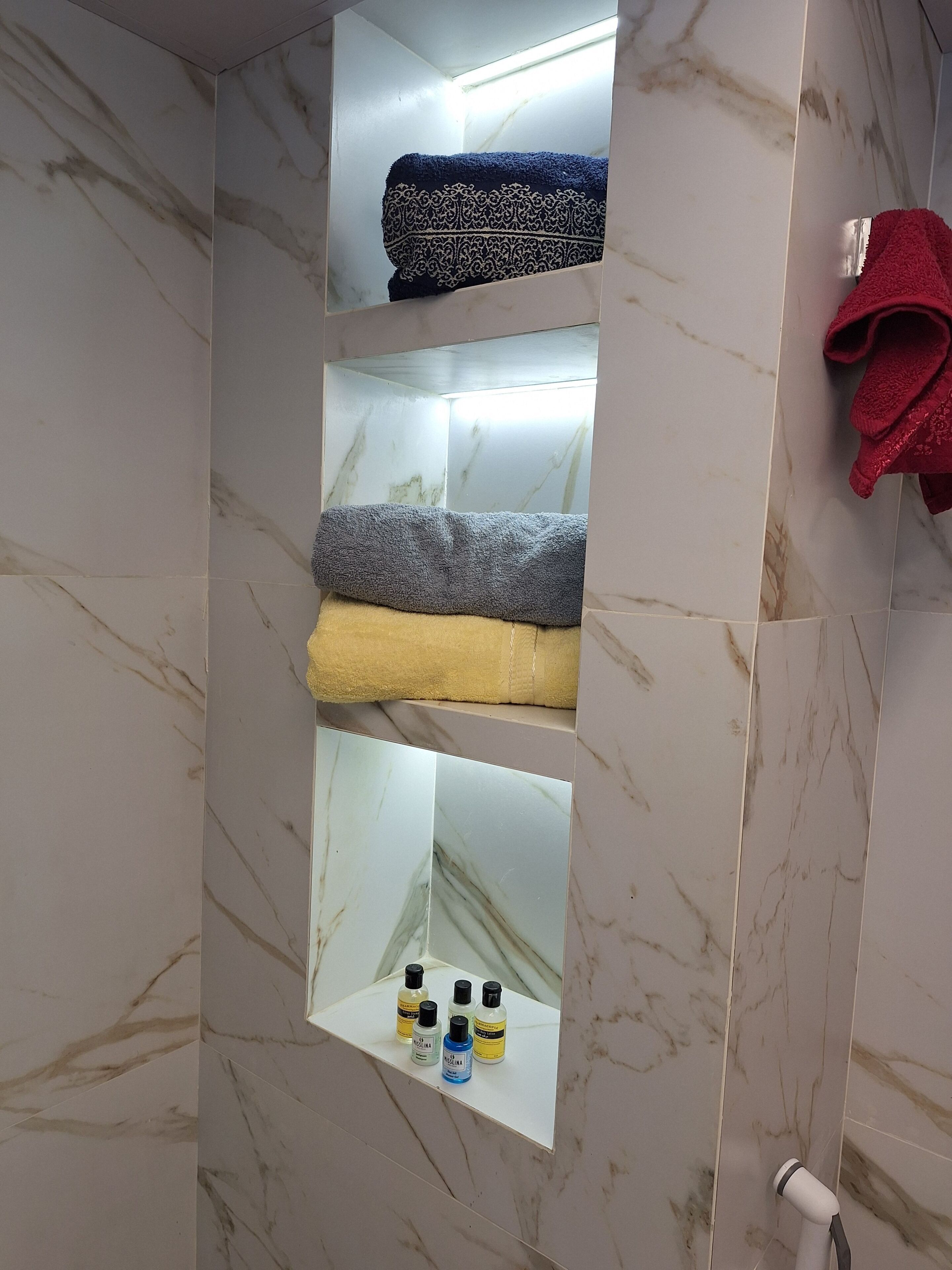 Um banheiro com paredes de mármore, um espelho e uma prateleira com toalhas e produtos de higiene pessoal.