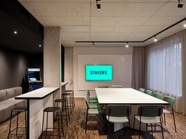 Uma sala de conferências moderna com uma mesa comprida, várias cadeiras, um sofá e um letreiro de neon com a palavra "STAYERY".