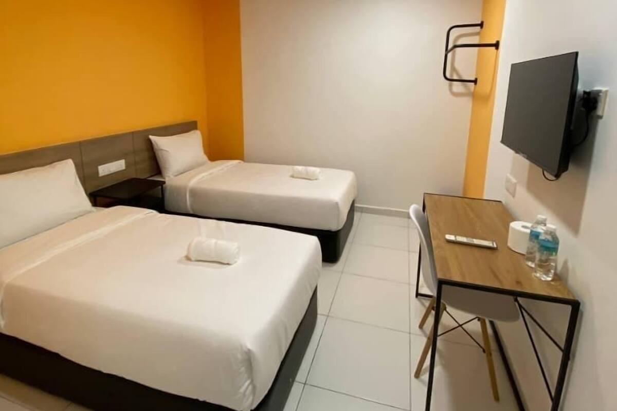 Quarto de hotel com duas camas, uma mesa, uma televisão e uma garrafa de água.