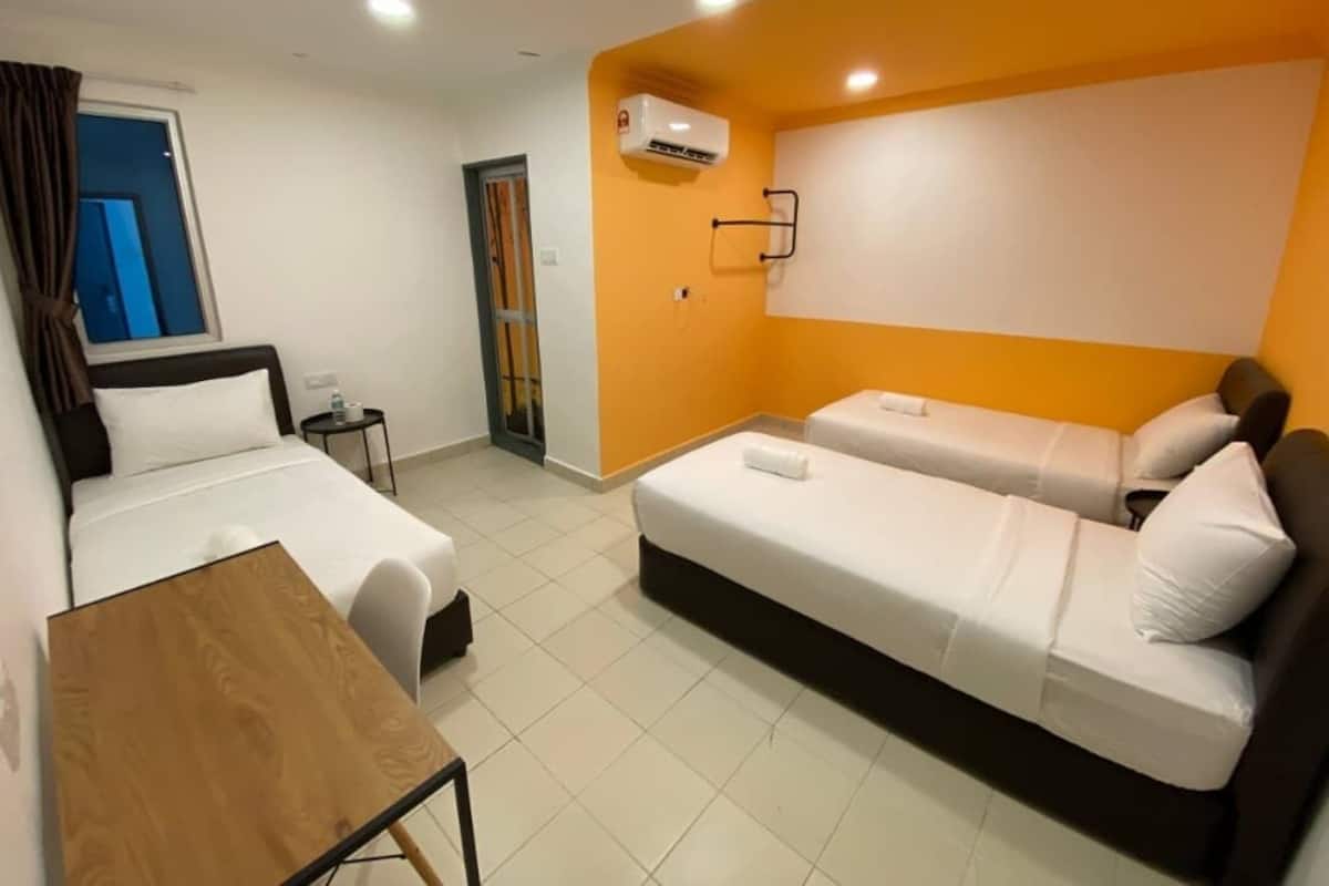 Quarto de hotel com duas camas, uma pequena mesa, ar condicionado e uma janela com cortinas.