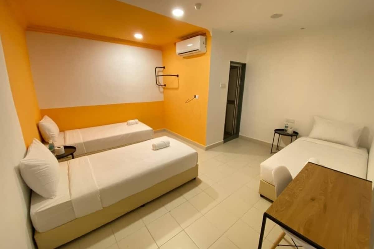Quarto de hotel compacto com sofá-cama, uma cama individual, uma mesa de madeira e unidade de ar condicionado.