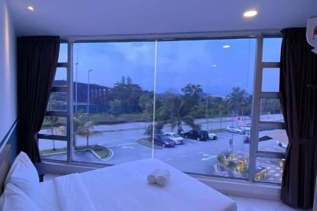 Quarto de hotel com uma cama grande, vista para um estacionamento e uma janela com cortinas.