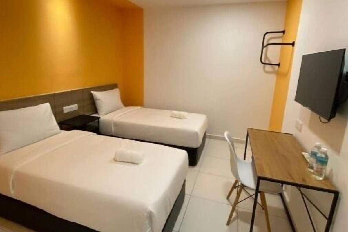 Quarto de hotel com duas camas, uma mesa, uma cadeira e uma televisão.
