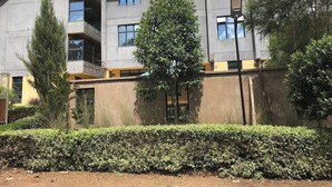 Um edifício moderno com vários andares, grandes janelas e uma sebe bem cuidada em primeiro plano.