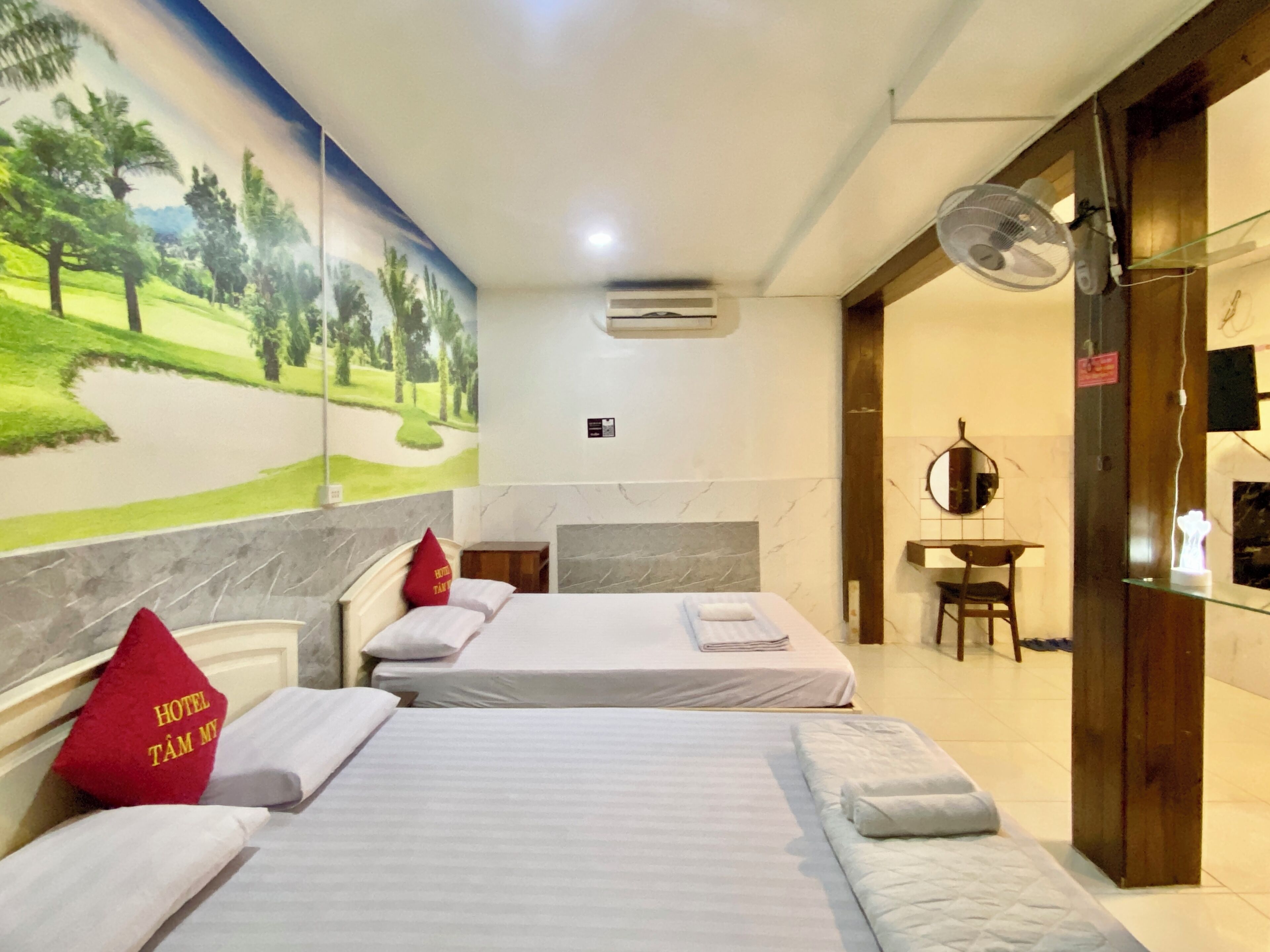 Quarto de hotel com duas camas, um mural representando um campo de golfe, uma escrivaninha de madeira e um espelho.