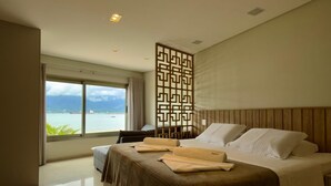 Quarto de hotel com uma cama grande, cabeceira de madeira, um biombo decorativo e vista para o mar.