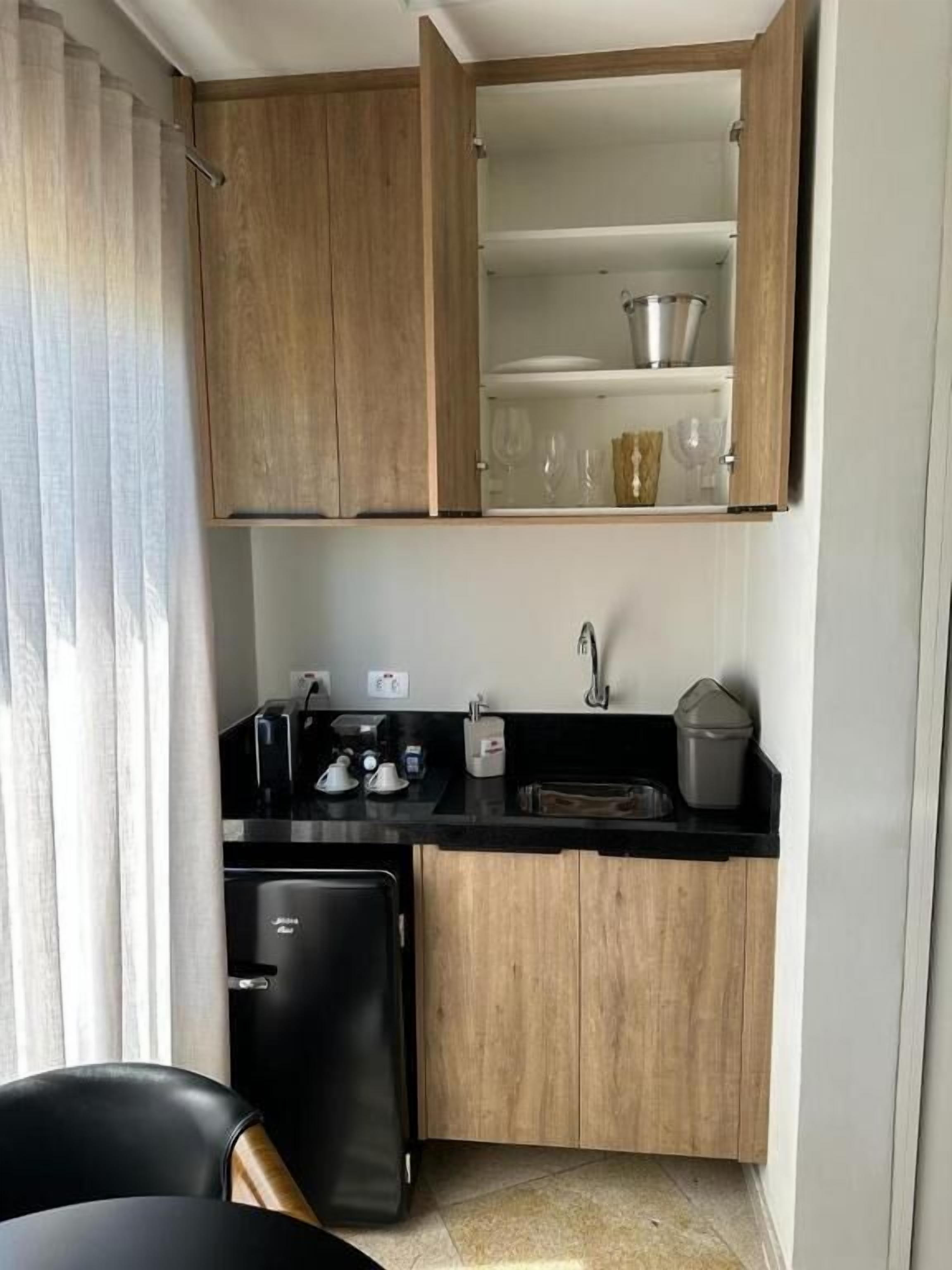 Uma cozinha compacta com armários de madeira, bancada preta, cafeteira e geladeira.