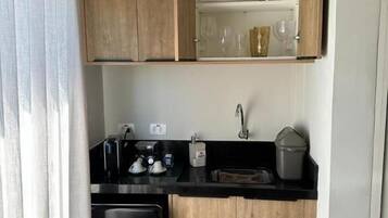 Uma cozinha compacta com armários de madeira, bancada preta, cafeteira e geladeira.