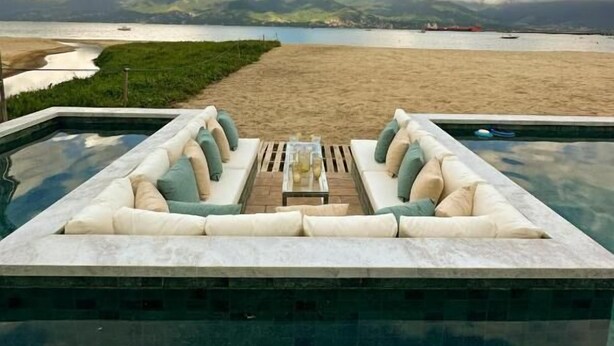 Área da piscina com vista para uma praia e montanhas.