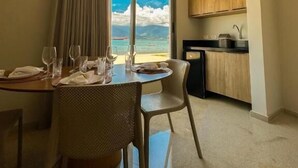 Uma sala de jantar com mesa posta para quatro, vista para o mar e área de cozinha com armários de madeira.