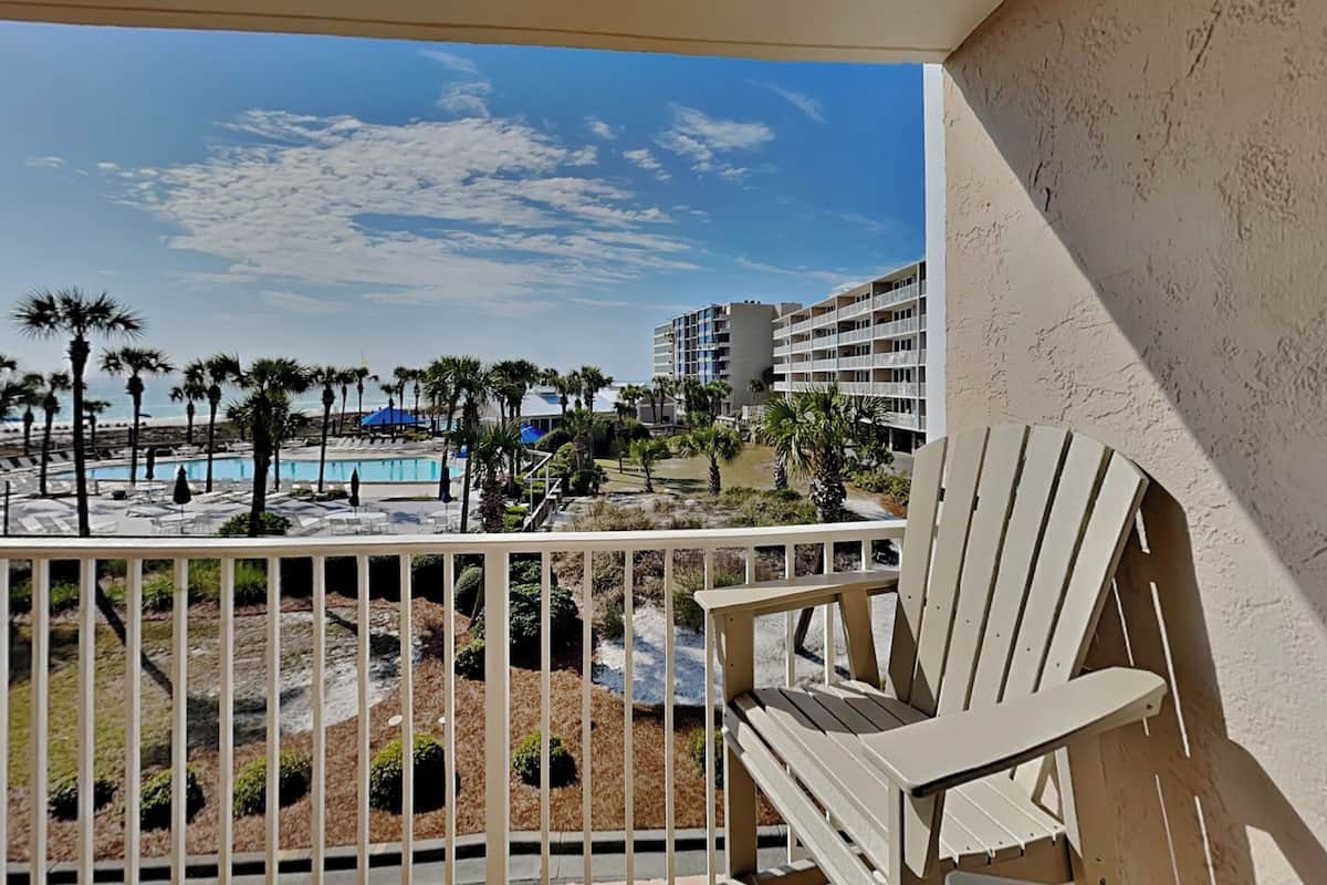 Uma varanda com vista para uma piscina, palmeiras e um edifício ao fundo.