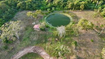 Vista aérea de uma área rural com um lago, uma construção pequena com telhado vermelho e árvores espalhadas.