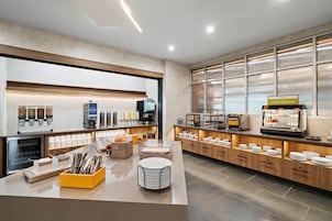 Uma área de café da manhã moderna com estação de autoatendimento, máquinas de café e vitrine de sanduíches.