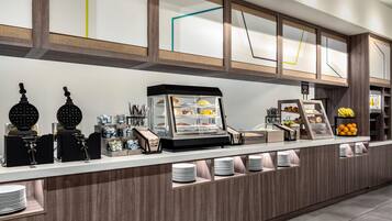 Um balcão de café da manhã moderno com uma máquina de café, uma vitrine com doces e uma cesta de frutas.