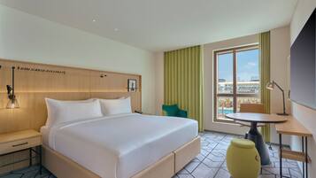 Quarto de hotel com uma cama grande, uma escrivaninha, uma cadeira, uma mesinha e vista para a cidade.