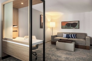 Quarto de hotel com uma cama, uma escrivaninha, uma cadeira, um sofá, um abajur e um quadro na parede.