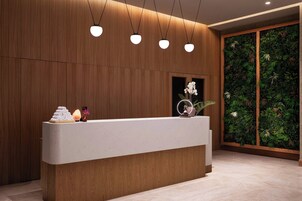 Uma receção com painel de madeira, um arranjo de plantas na parede e um pequeno vaso com flores.