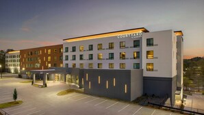 Um hotel Courtyard by Marriott com fachada moderna, vários andares e uma entrada bem iluminada.