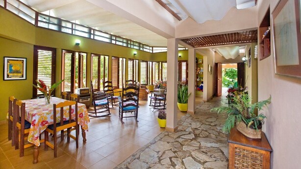 Uma sala de jantar ampla com pé direito alto, janelas grandes e piso de pedra.