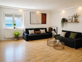 Uma sala de estar moderna com dois sofás pretos, uma mesa de centro de vidro e uma grande pintura abstrata na parede.