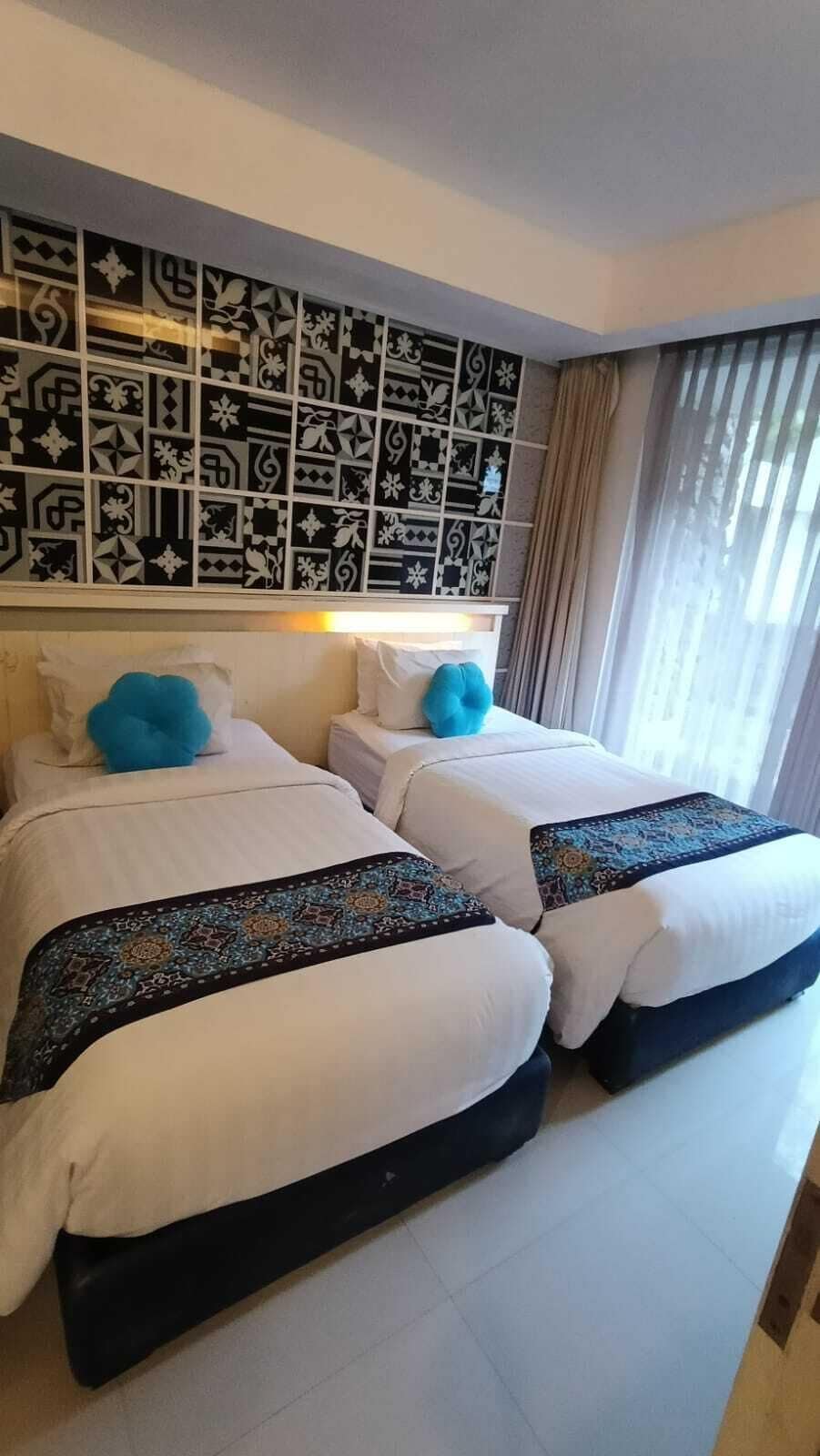 Quarto de hotel com duas camas, um painel decorativo e uma janela com cortinas.