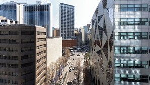Paisagem urbana com edifícios modernos e altos, um estacionamento e um edifício com fachada geométrica marcante.