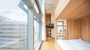 Quarto de hotel moderno com uma grande janela, uma cama, uma TV e piso de madeira.